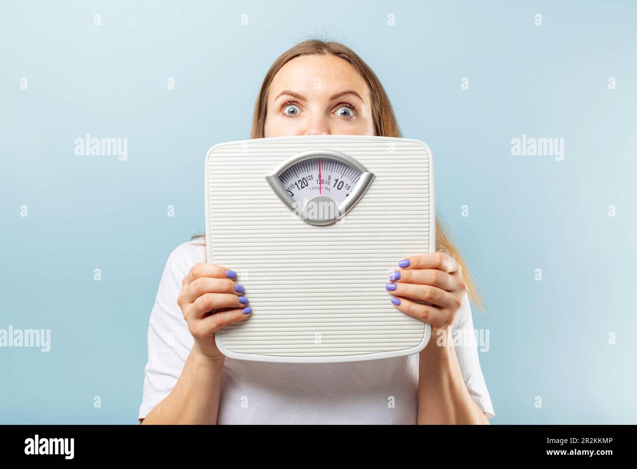 Scared young brunette woman in white t-shirt holding scales on blue ...