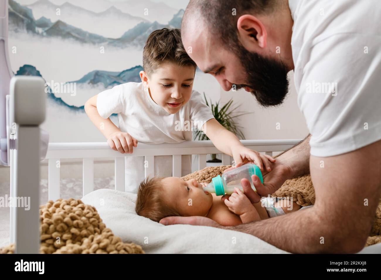 Father and big older brother feed newborn infant with formula, baby in ...