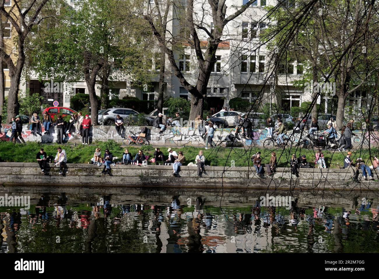 Frühling in Berlin. Junge Leute sitzen in Gruppen am Landwehrkanal in ...