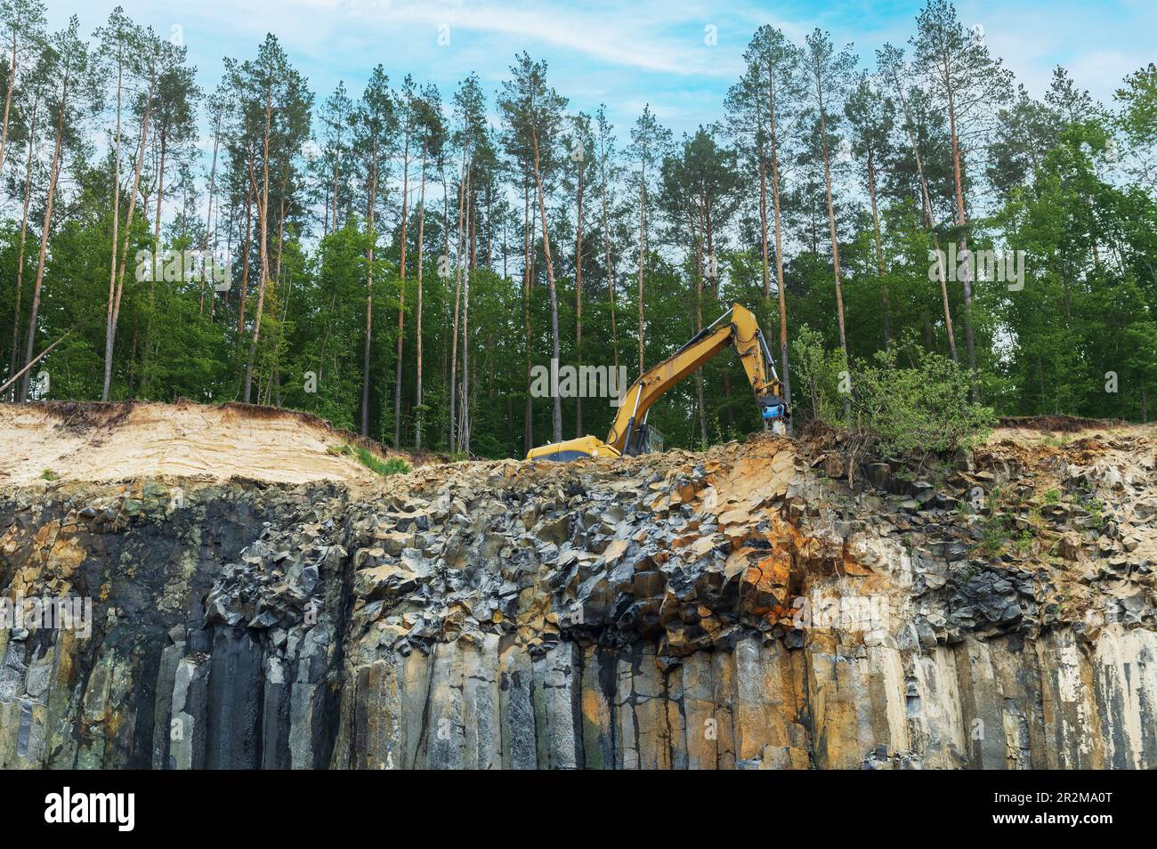Basalt mining. Yellow excavators in a basalt quarry near the forest ...