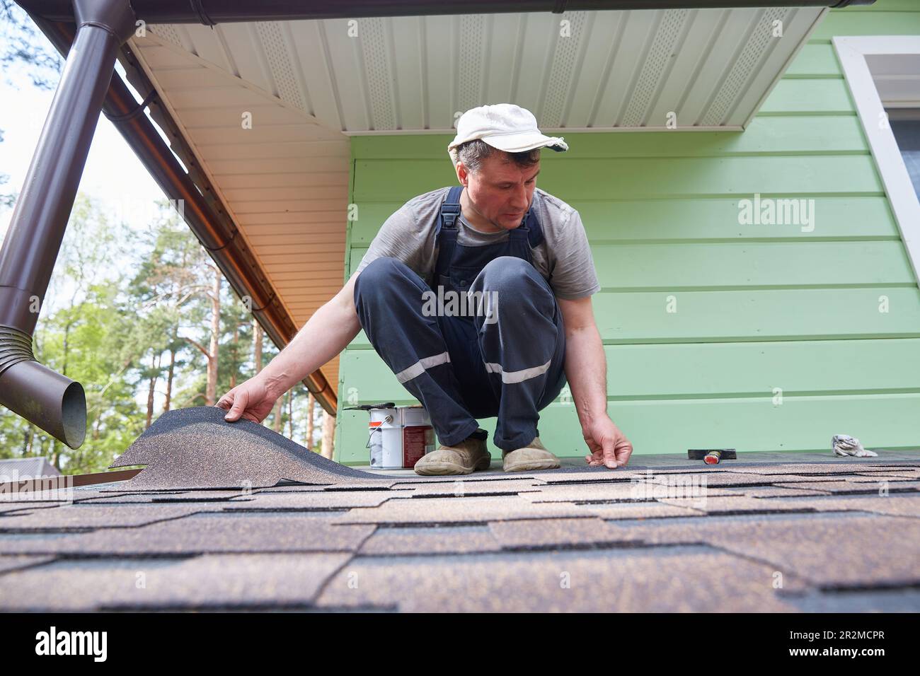 A worker installs a soft roof on the roof of a country house. Made of ...