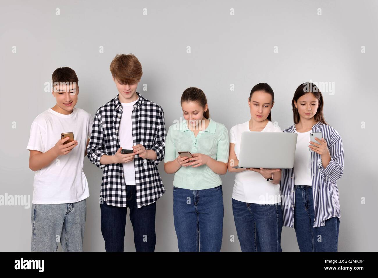 Group of happy teenagers using different gadgets on light grey ...