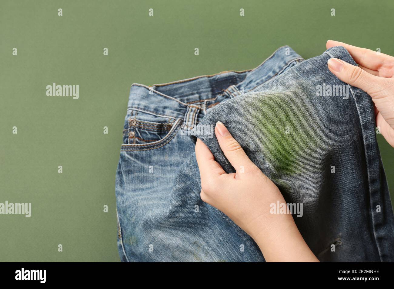 Woman holding jeans with stain on green background, closeup. Space for ...