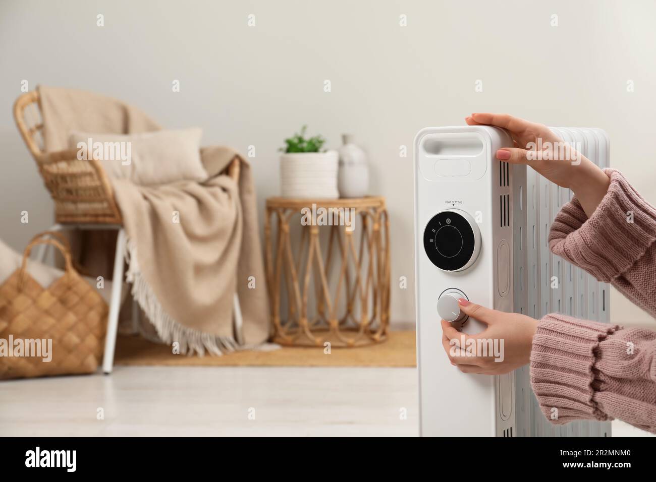Woman adjusting temperature on modern portable electric heater indoors ...