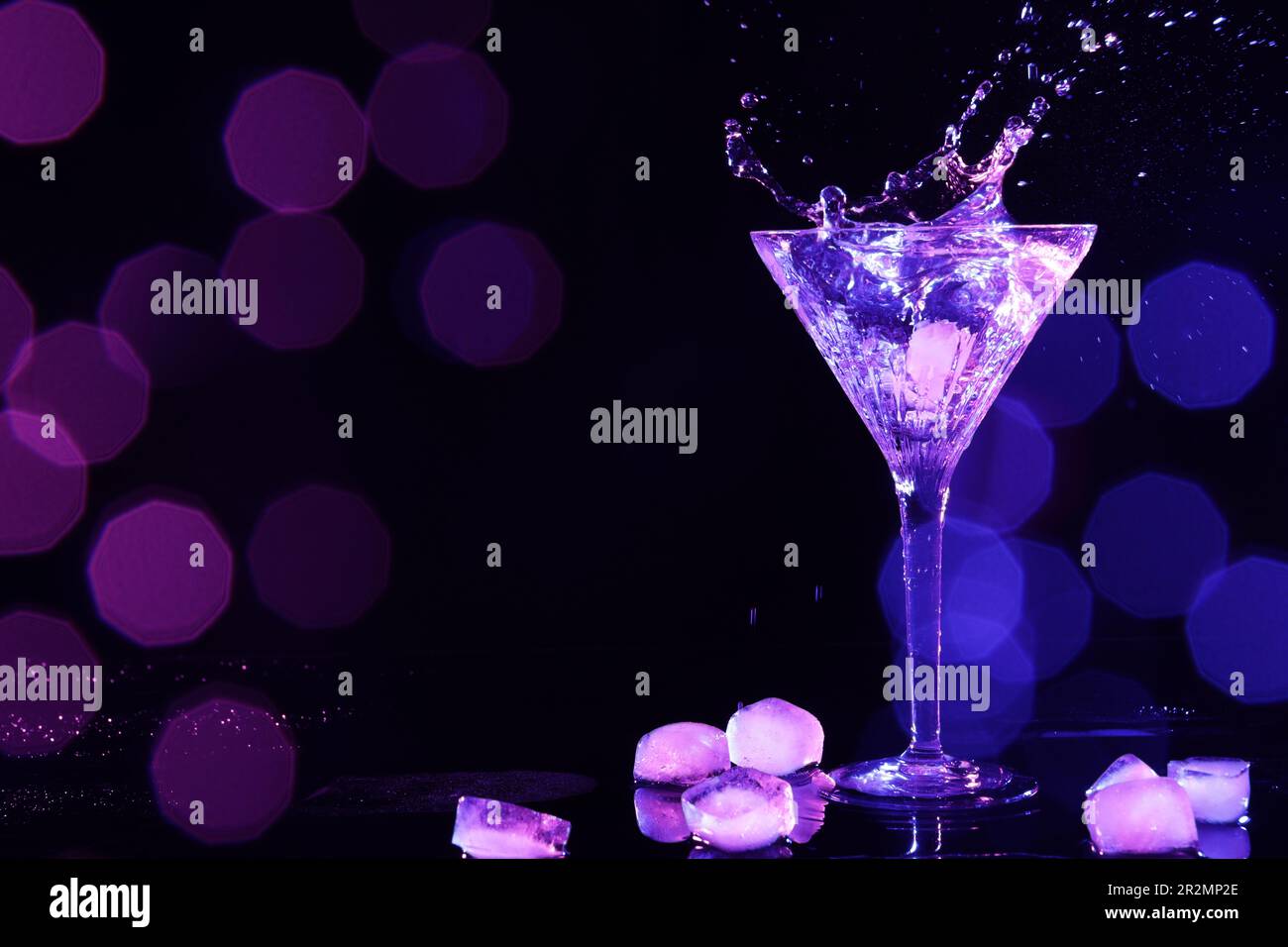 Glass of martini with ice and splashes in neon lights on dark ...