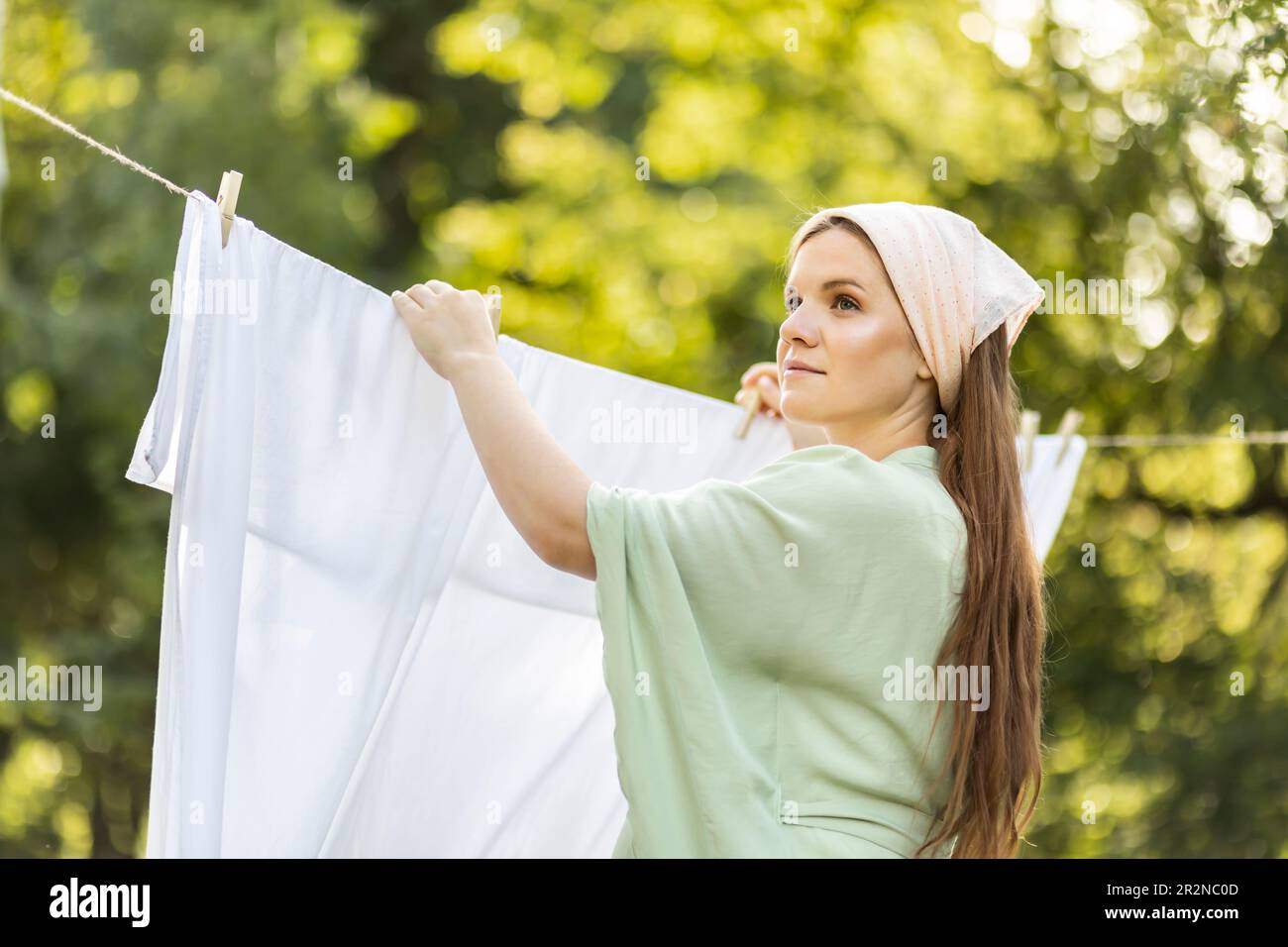 Young pretty white woman hanging up laundry on clothes line outside ...