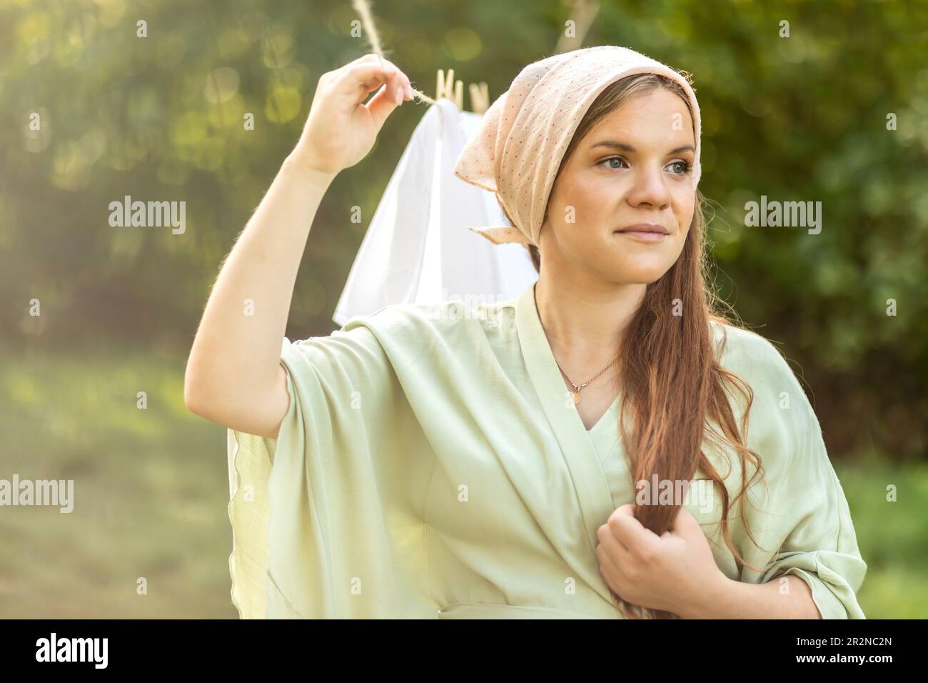Portrait of young pretty white woman hanging up laundry on clothes line ...