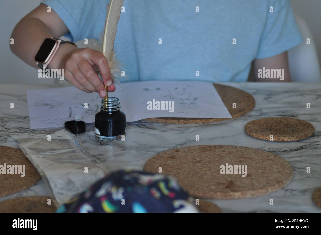 A girl using a feather quill and ink to write and draw on white paper ...
