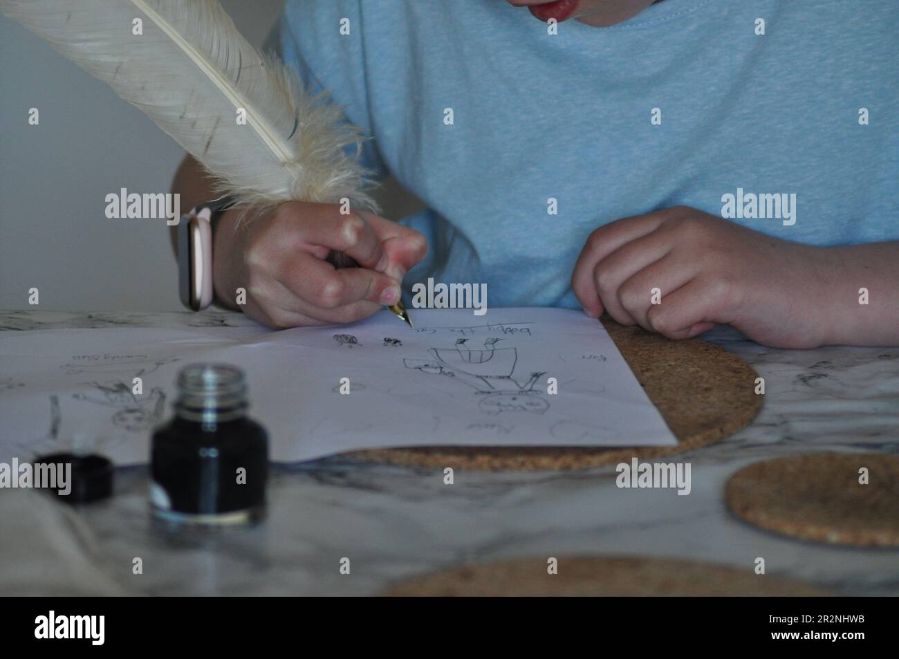 A girl using a feather quill and ink to write and draw on white paper ...