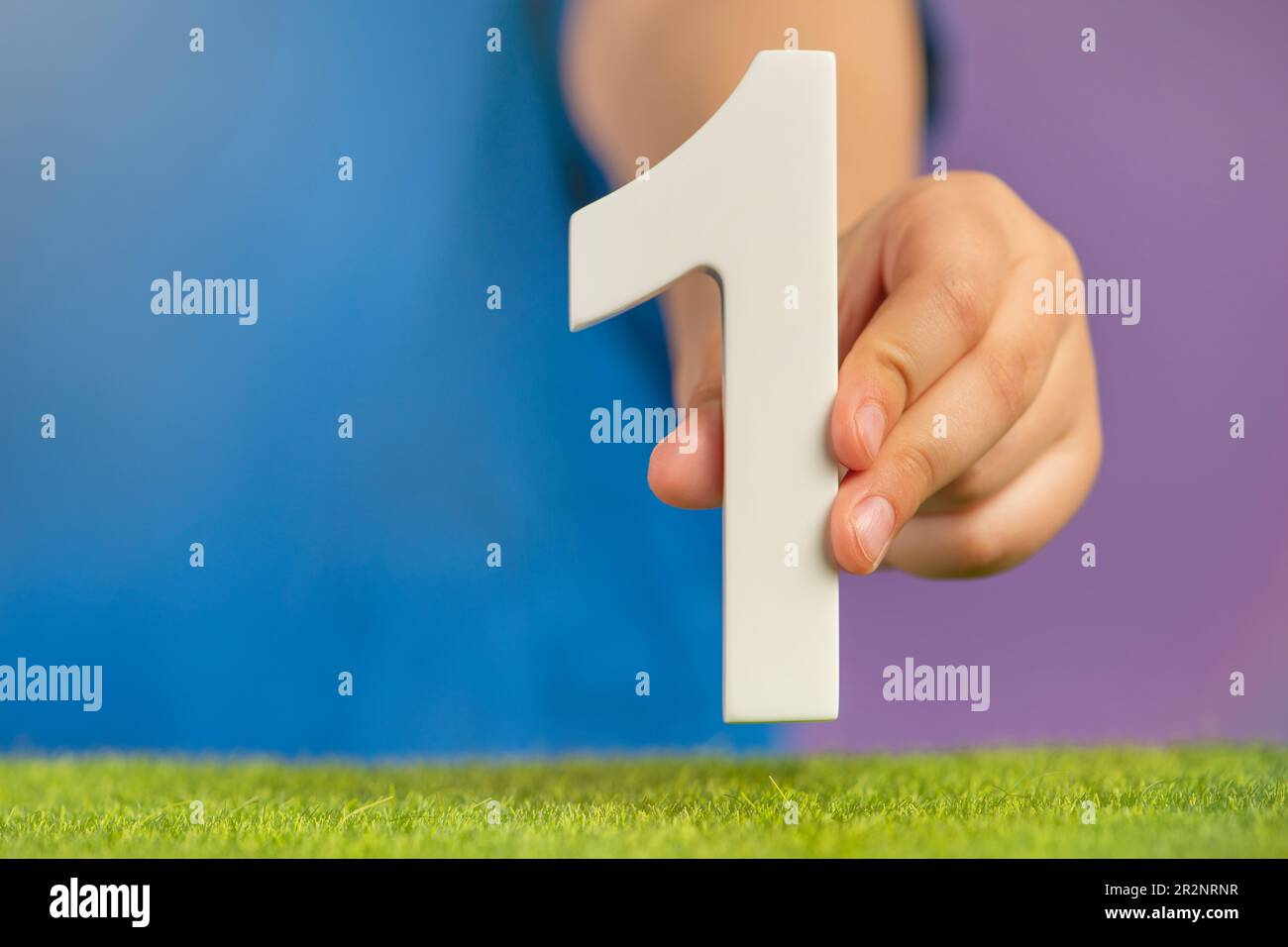 Number 1 in hand. Hand holding white number one over green grass and ...
