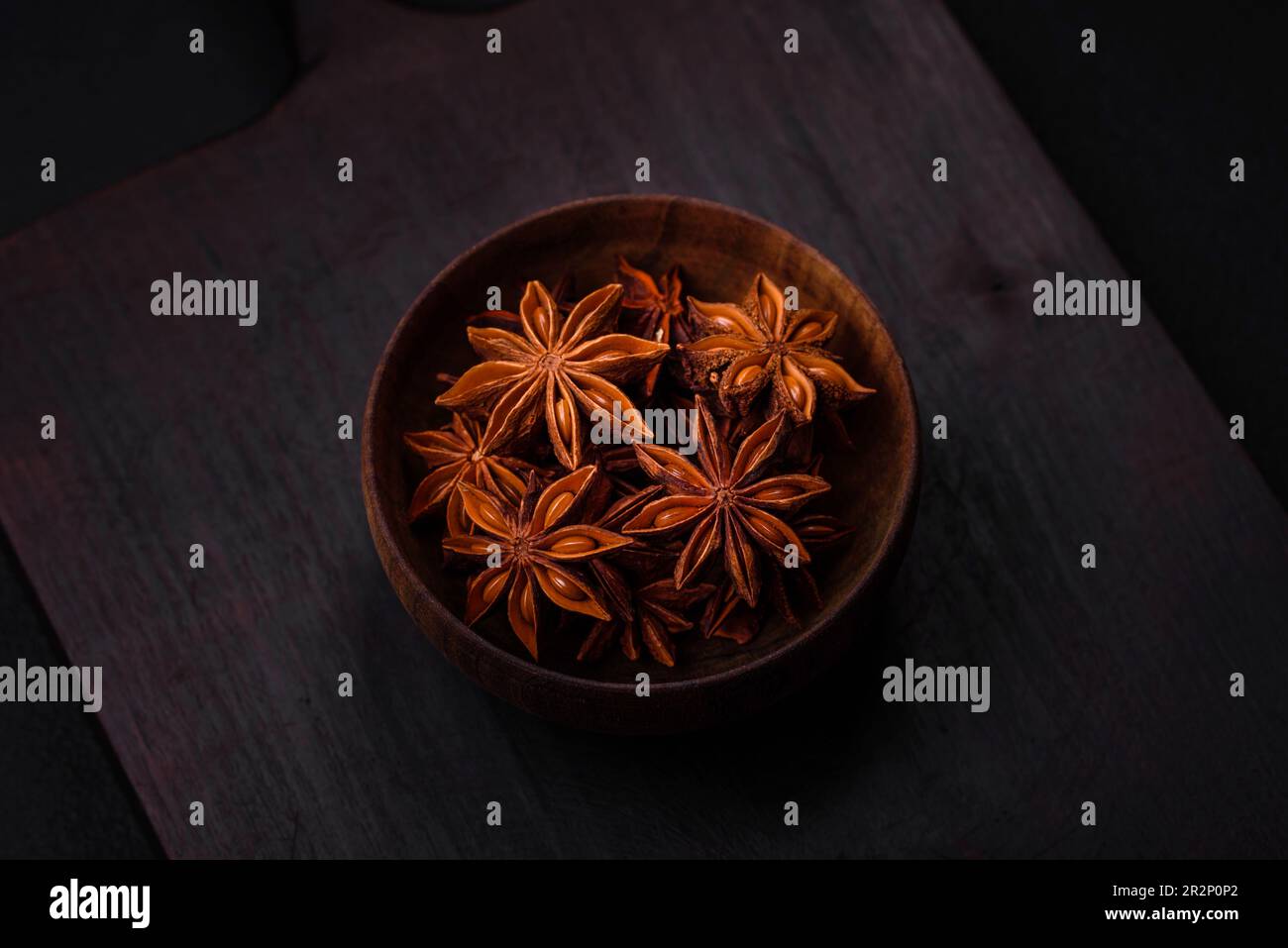 Star shaped spice star anise in a wooden round bowl on a dark concrete ...