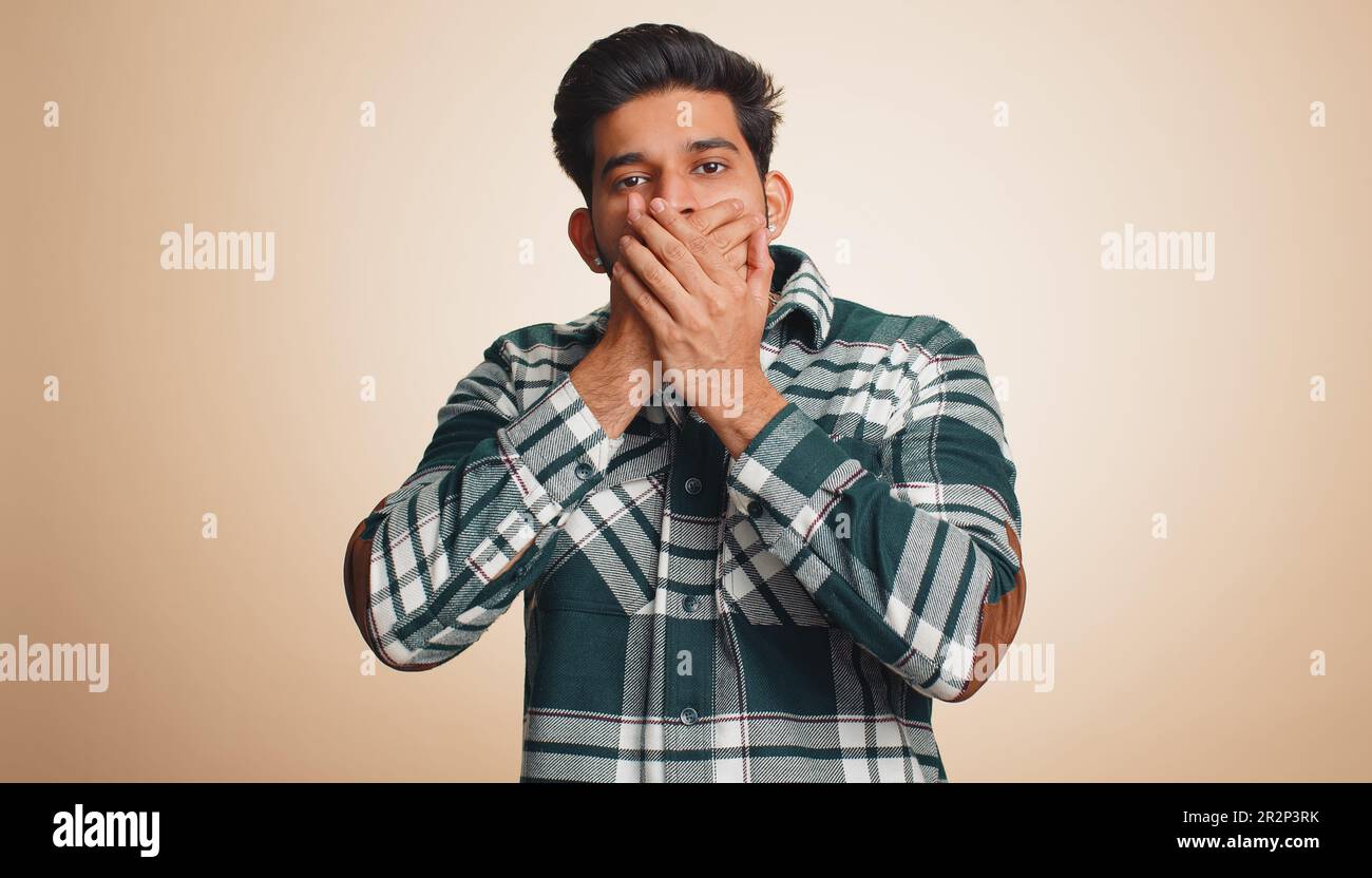 I will not say anyone. Frightened indian man closing mouth with hands ...