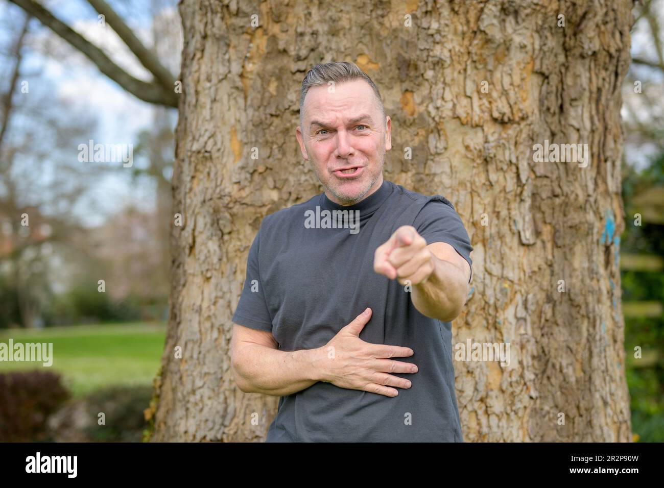 Gray-haired man standing in front of a tree in the park and ...