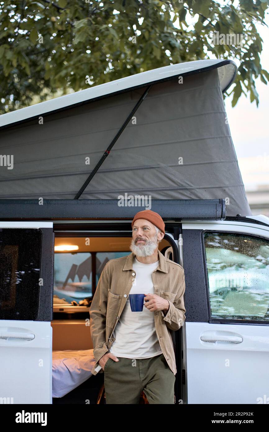 Older man traveler standing near rv camper van drinking coffee enjoying ...
