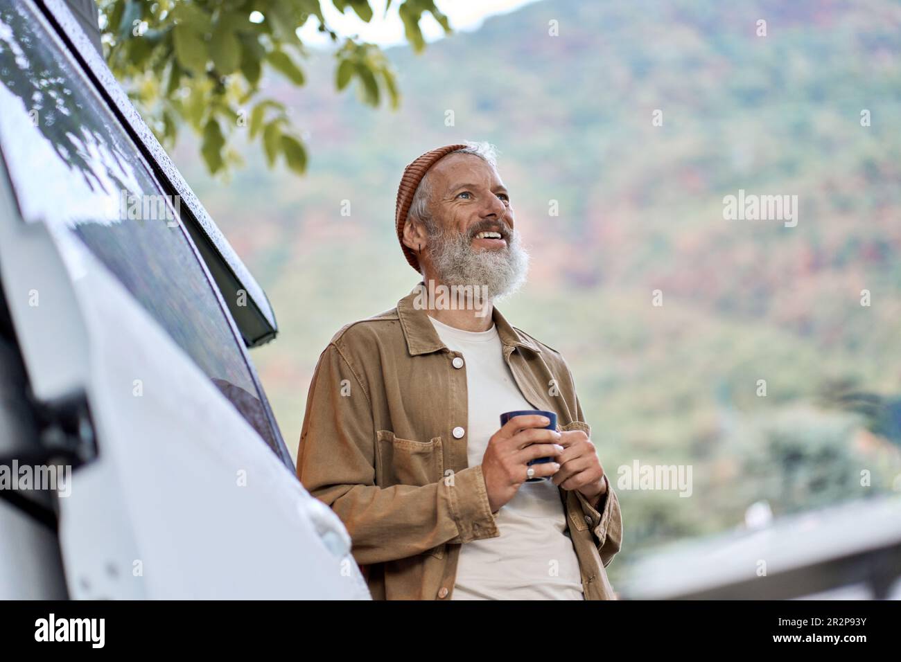 Happy old man traveler standing near camper van drinking coffee ...