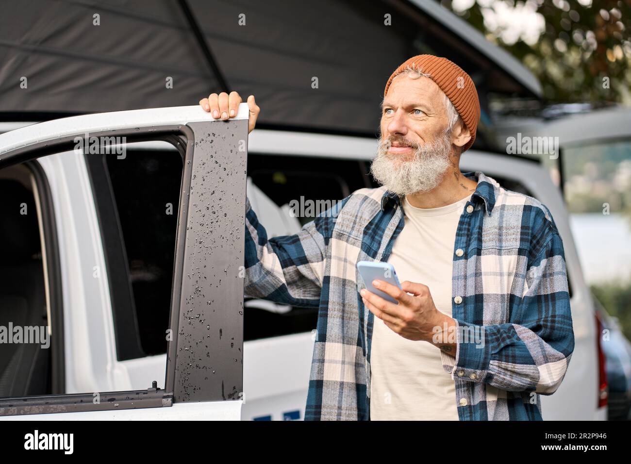 Older man standing near rv camper van on vacation using mobile phone ...