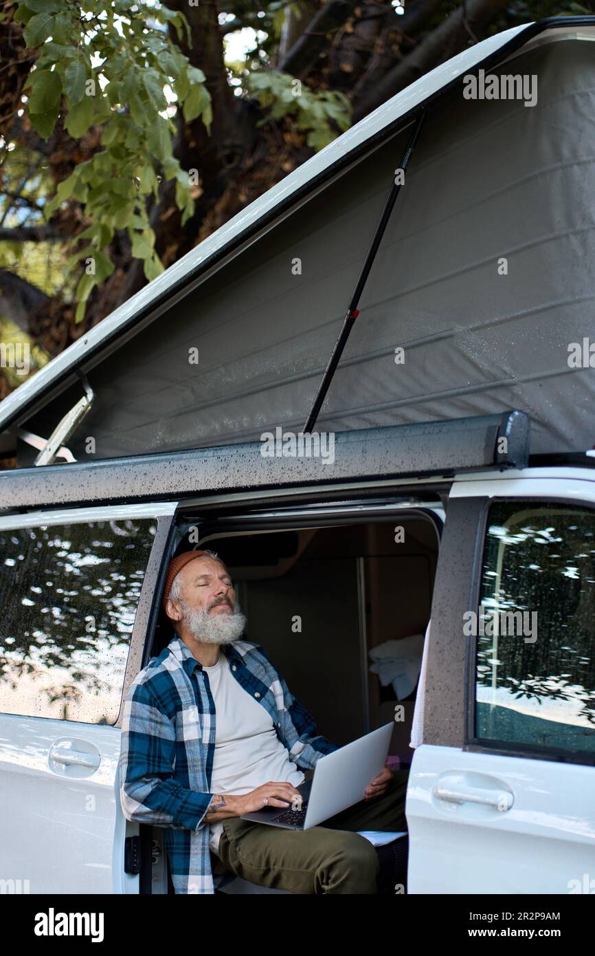 Calm older man traveler sitting in camper van using laptop in camping ...