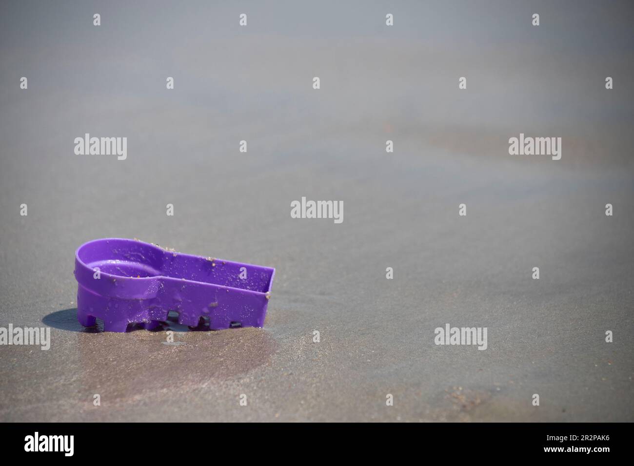 abandoned purple bucket on the sand at the beach, not being played with ...