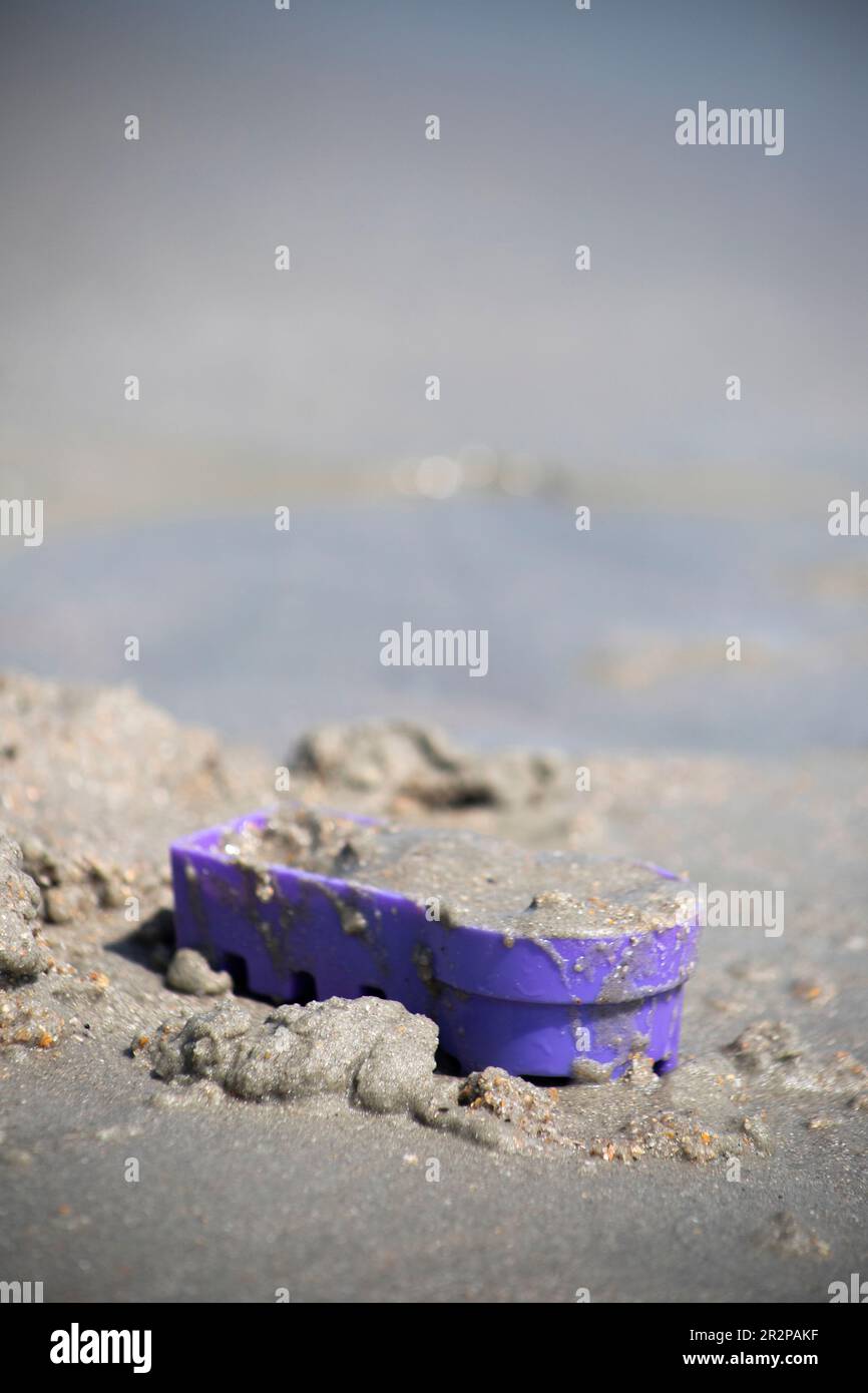 abandoned purple bucket on the sand at the beach, not being played with ...