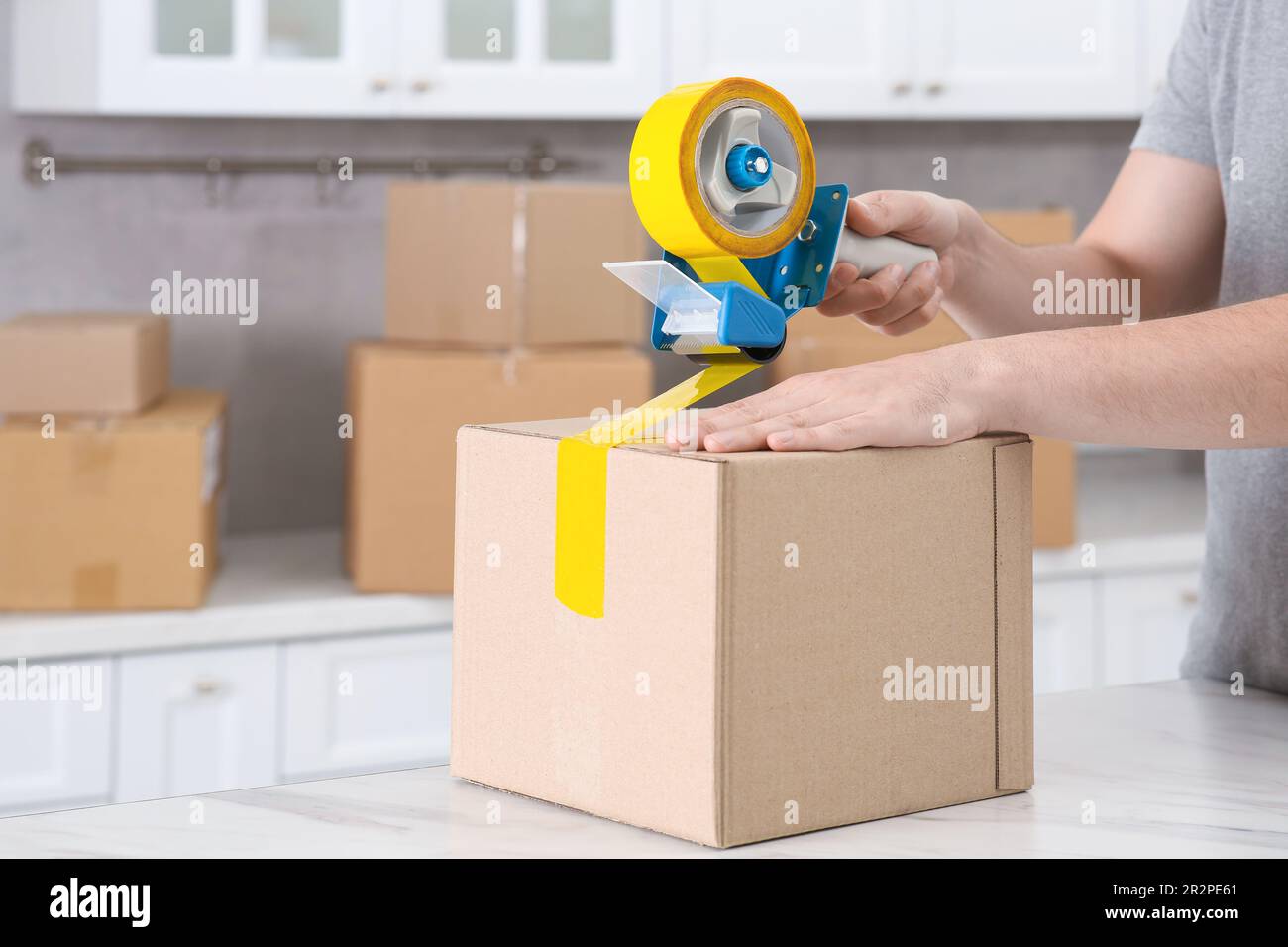 Man taping box with adhesive tape dispenser in kitchen, closeup Stock ...