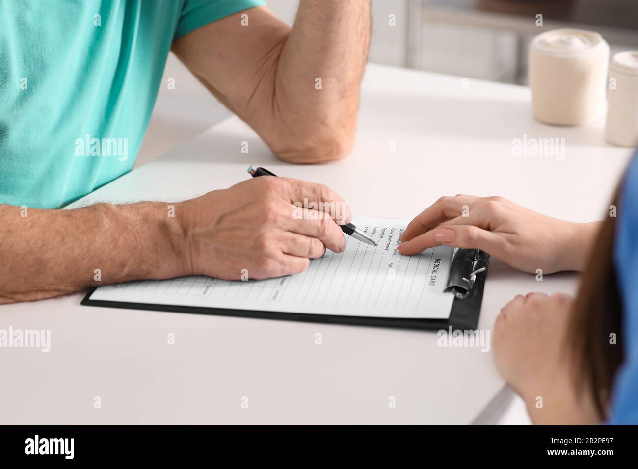 Doctor helping patient filling his medical card at table in clinic ...