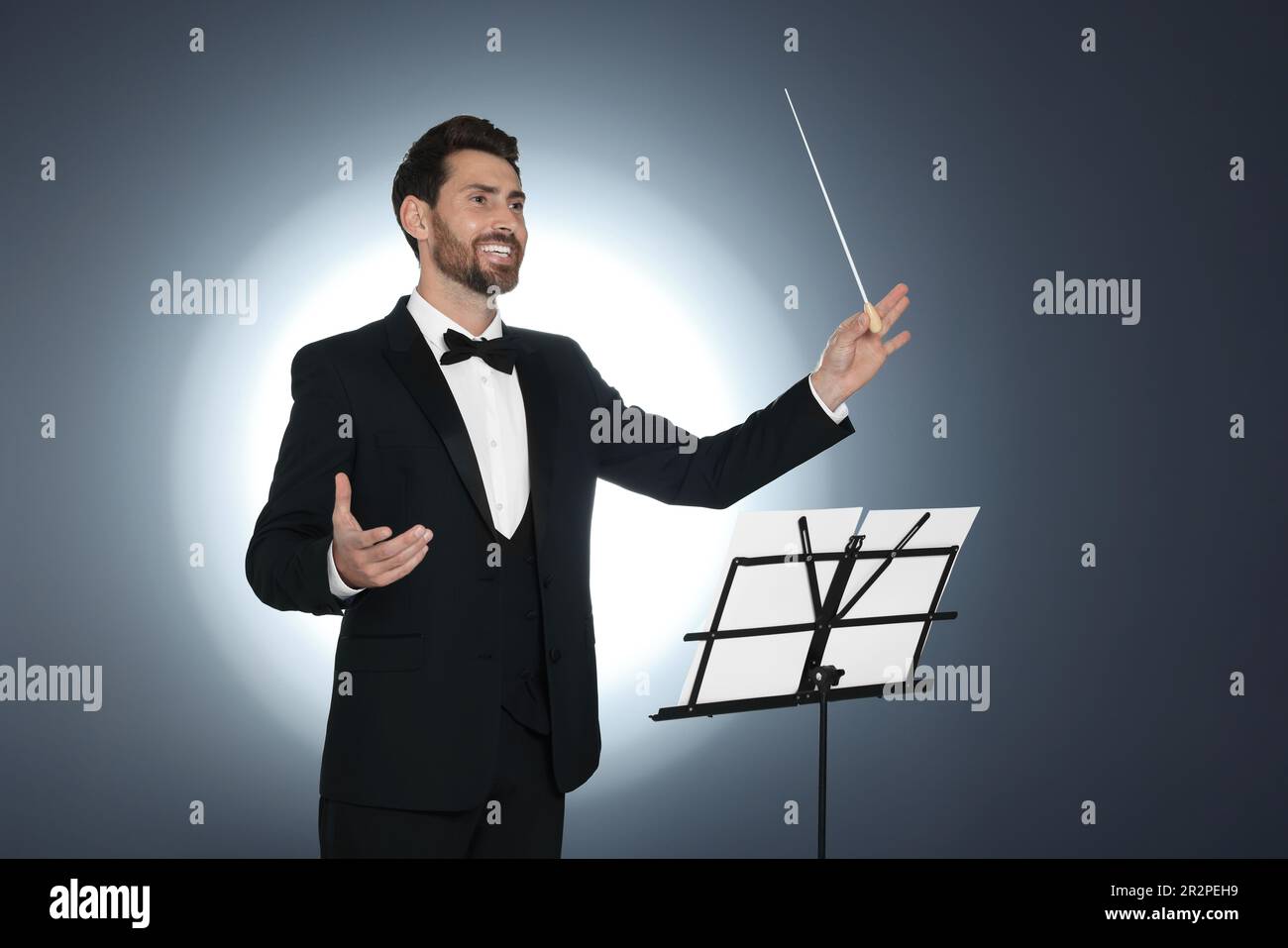 Happy professional conductor with baton and note stand on grey ...