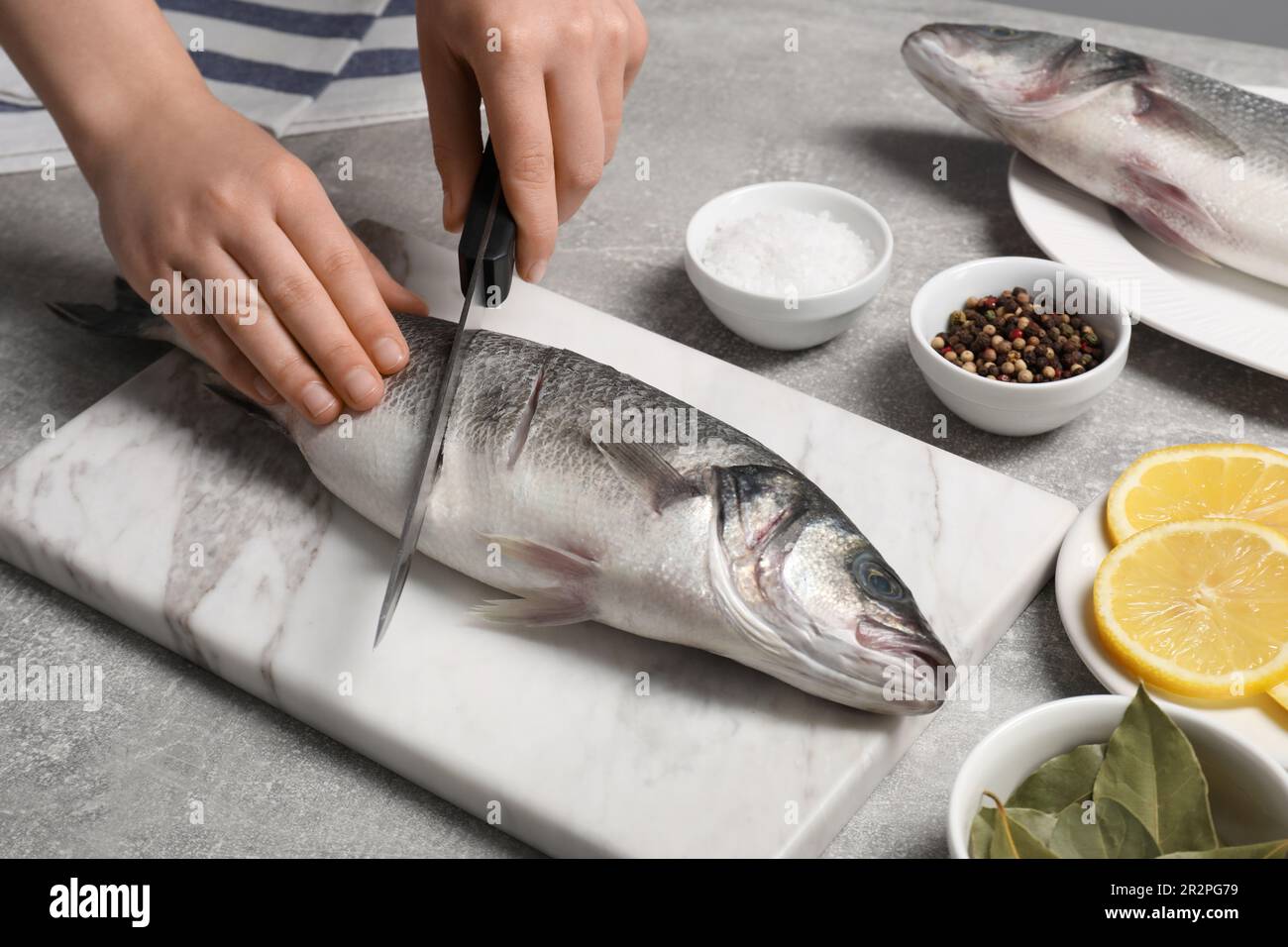 Woman cutting fresh raw sea bass fish at light gray table, closeup ...