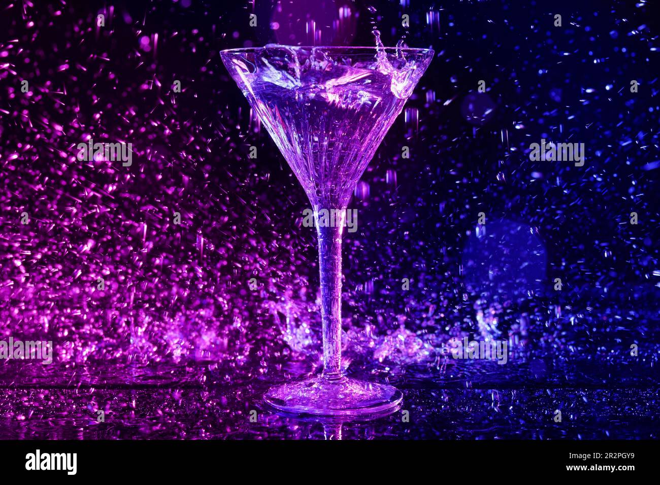 Glass of martini and splashes in neon lights on dark blue background ...