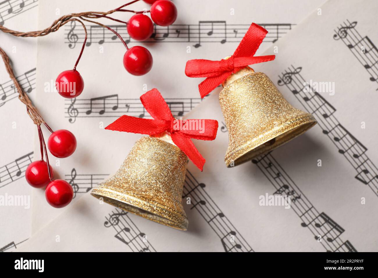 Golden shiny bells with red bows and decorative berries on music sheets ...