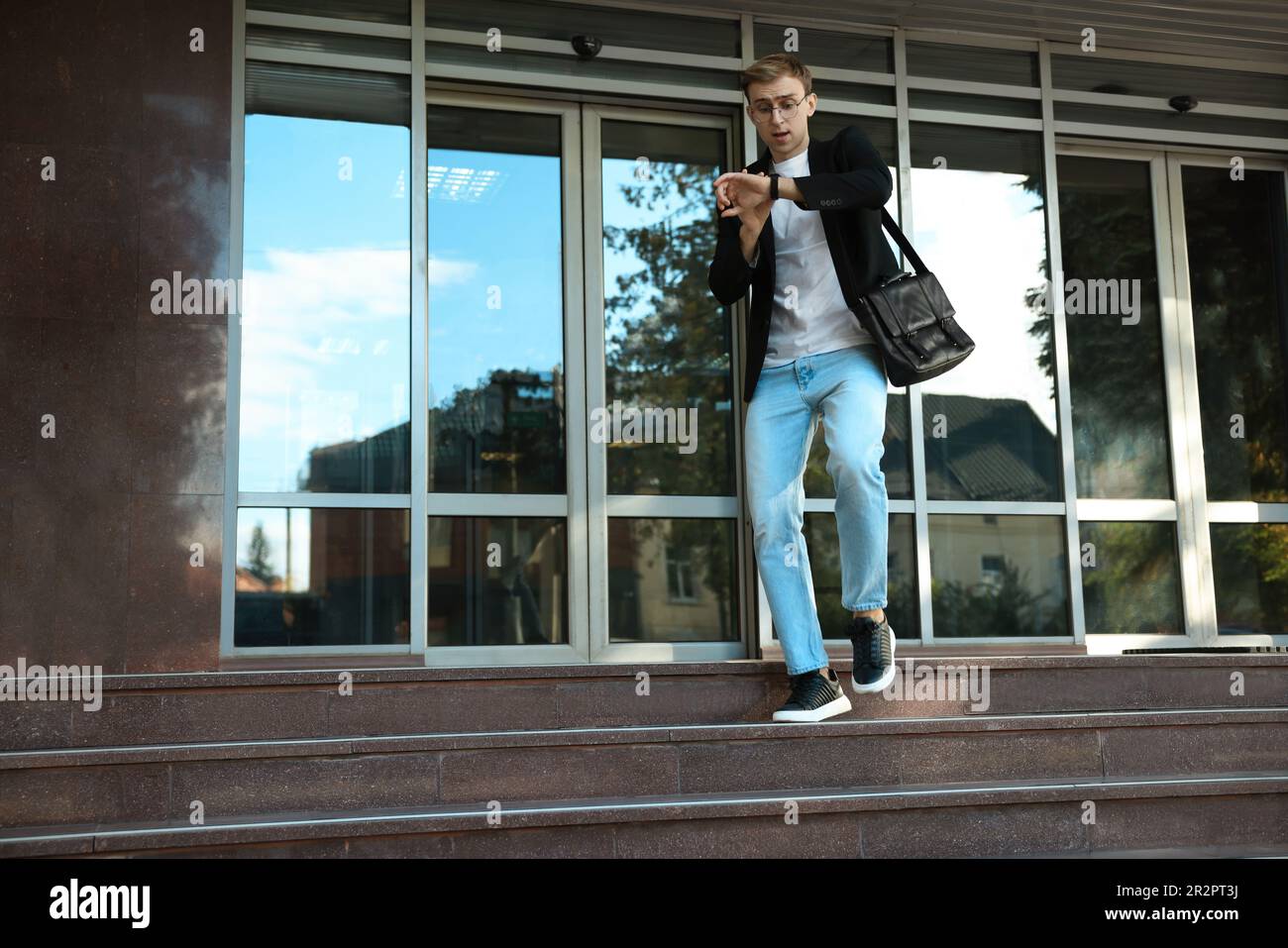 Emotional young man checking time while going down stairs near modern ...