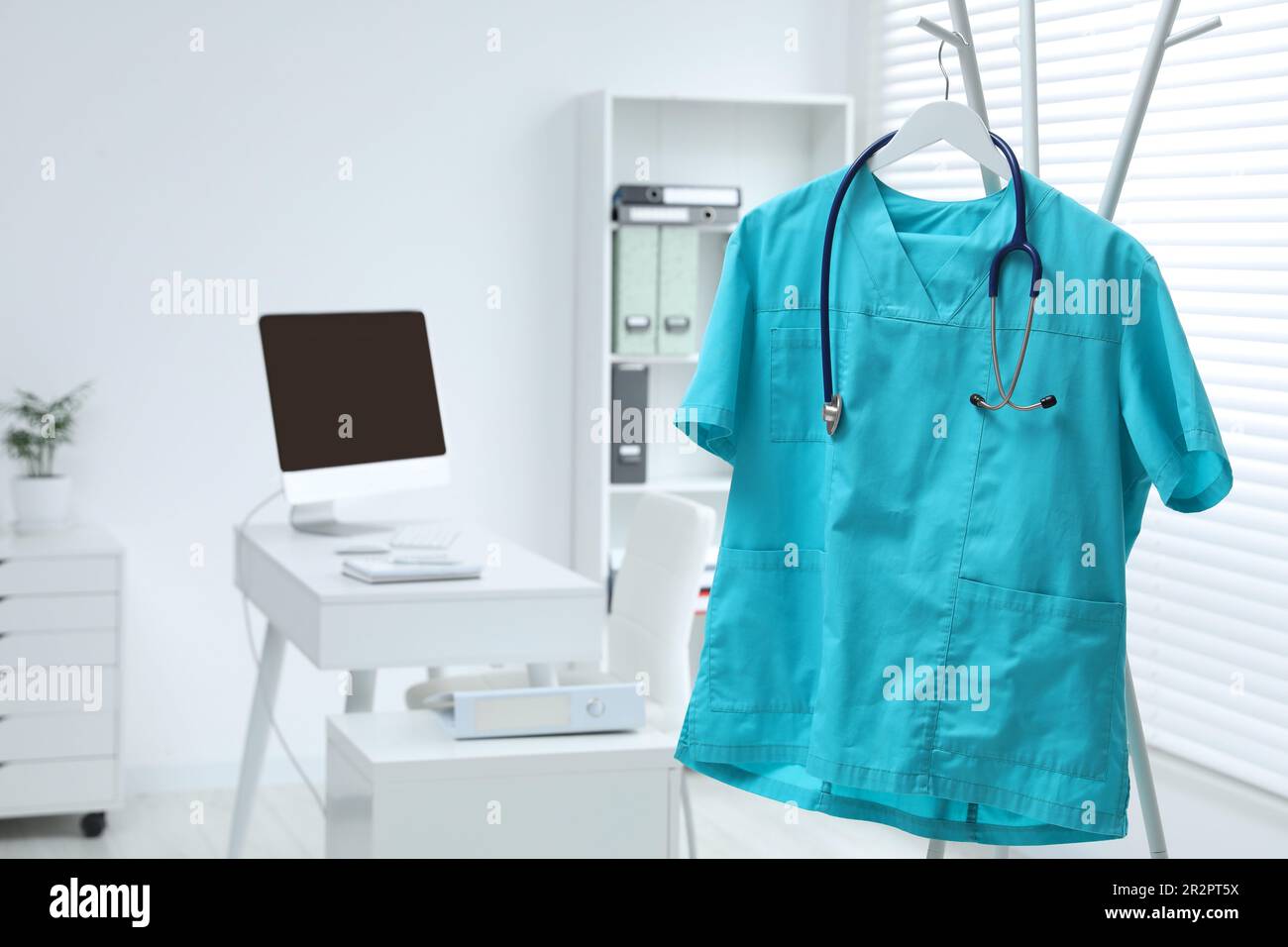 Turquoise medical uniform and stethoscope hanging on rack in clinic ...