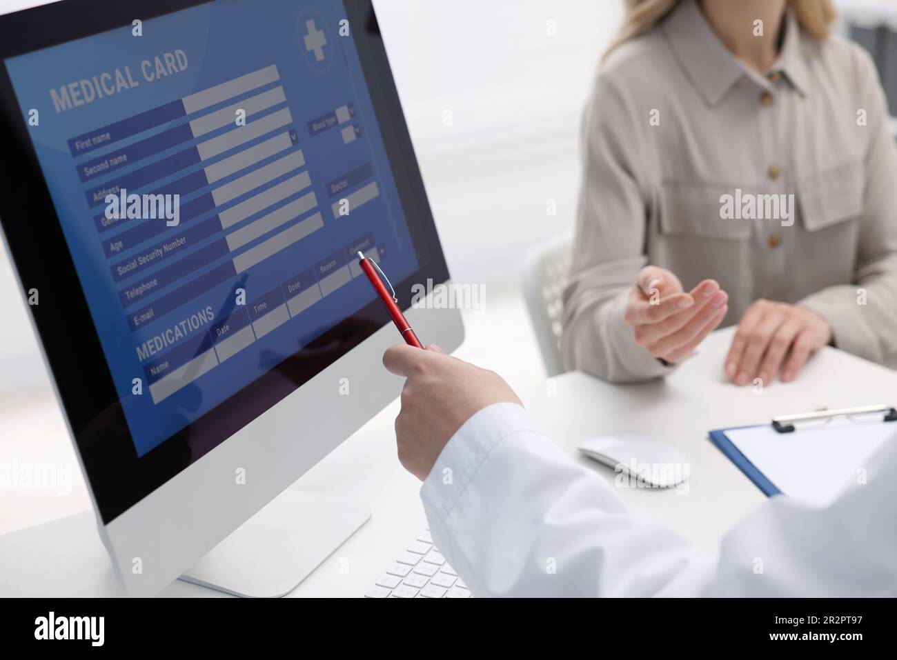 Doctor using computer to fill out patient's medical card at table in ...