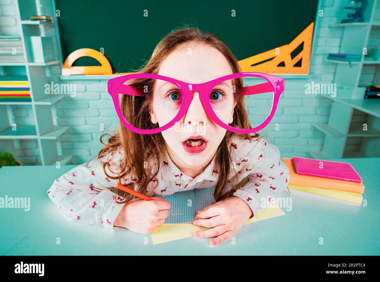 Funny geek surprised child school girl with fun glasses in classroom ...