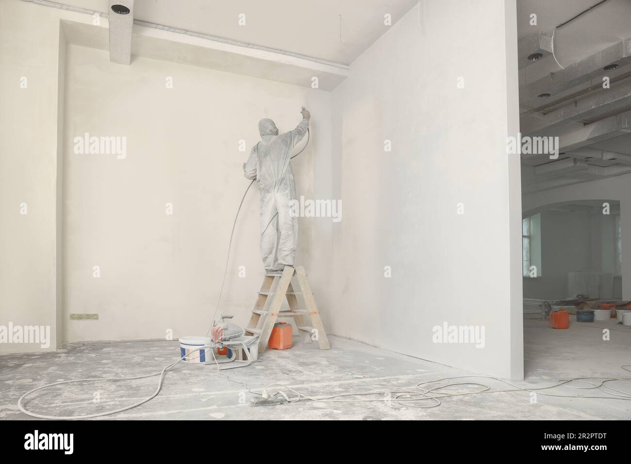 Decorator in uniform painting wall with sprayer indoors, back view ...