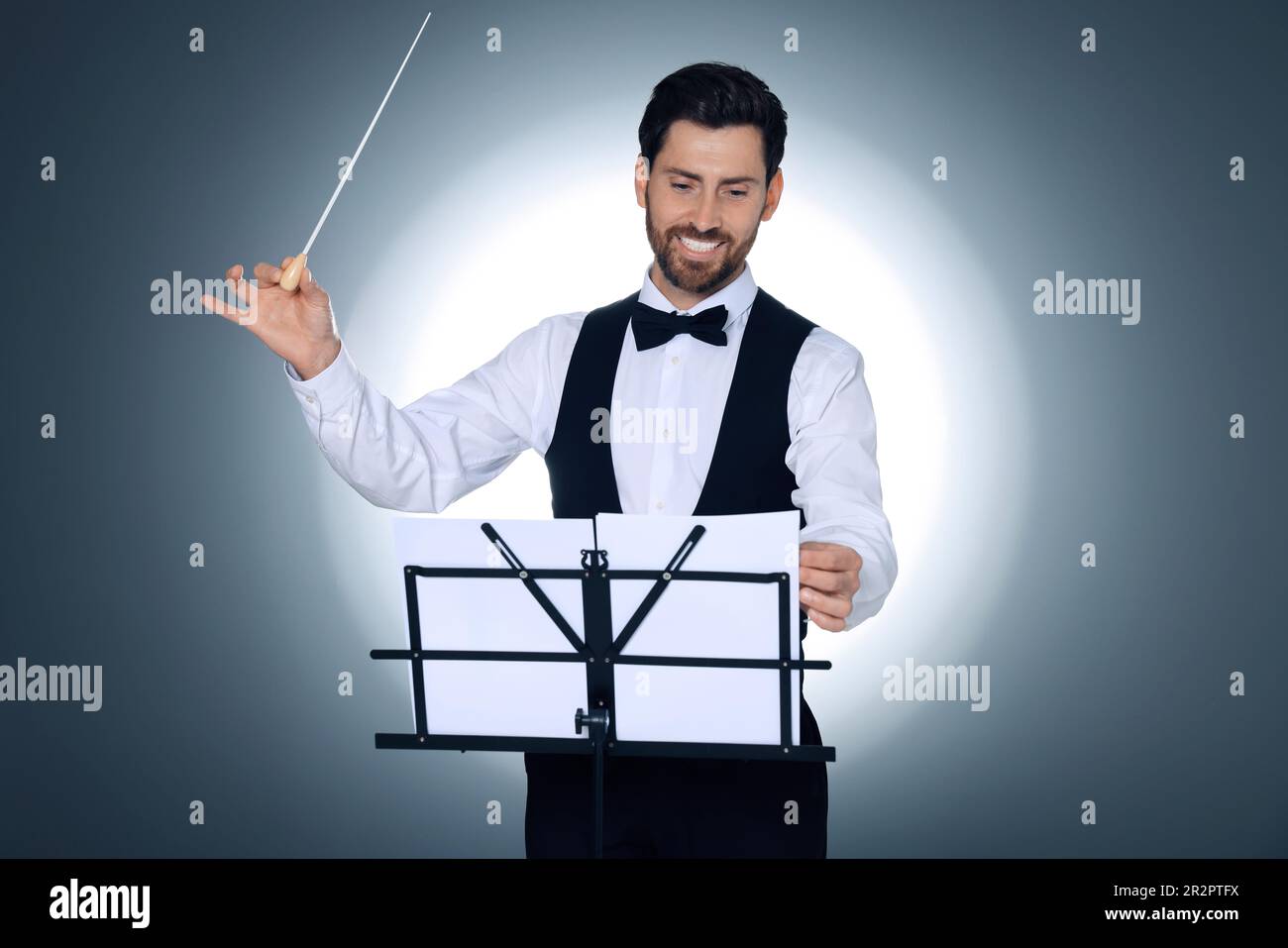 Happy professional conductor with baton and note stand on grey ...
