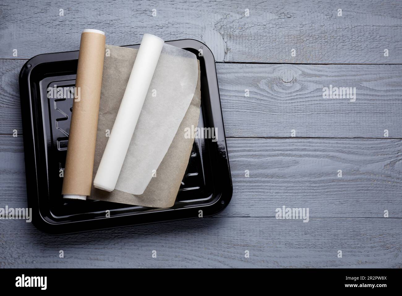 Rolls of parchment paper and baking pan on grey wooden table, top view ...