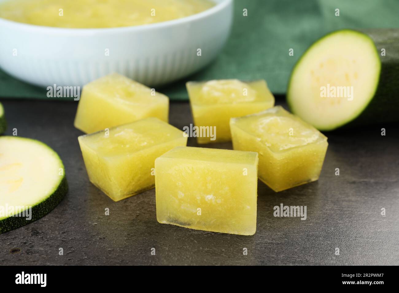 Frozen zucchini puree cubes and fresh zucchini on grey table, closeup ...