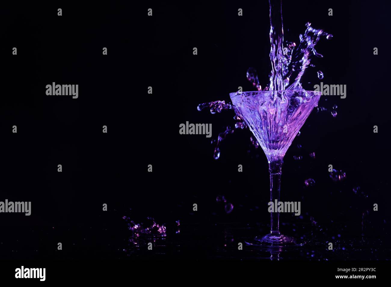 Pouring martini. Glass and splashes in neon lights on dark background ...