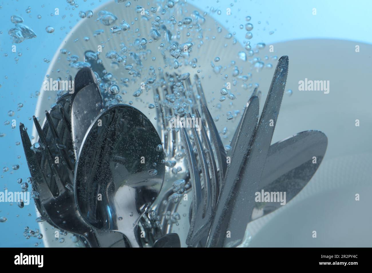 Washing silver cutlery and plates in water on light blue background ...