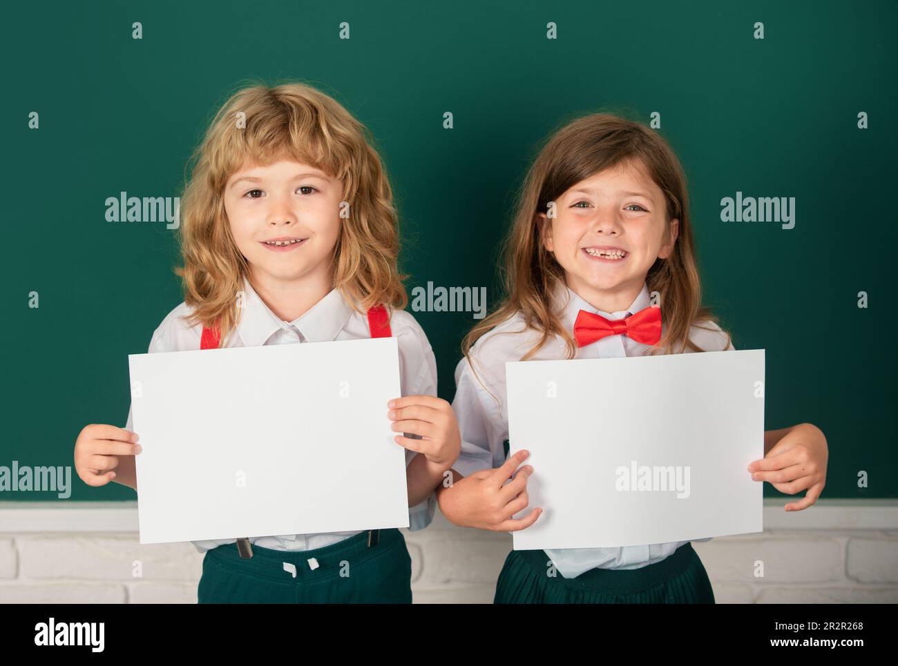 Two schoolkids holding white paper blank, poster with copy space ...