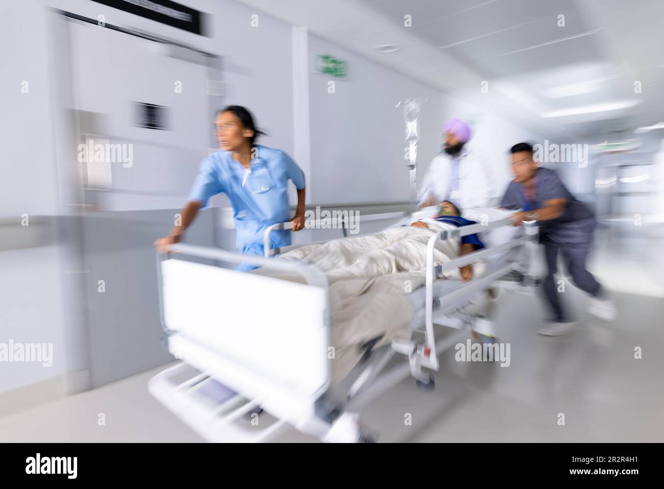 Diverse doctors urgently pushing patient lying in bed in corridor at ...