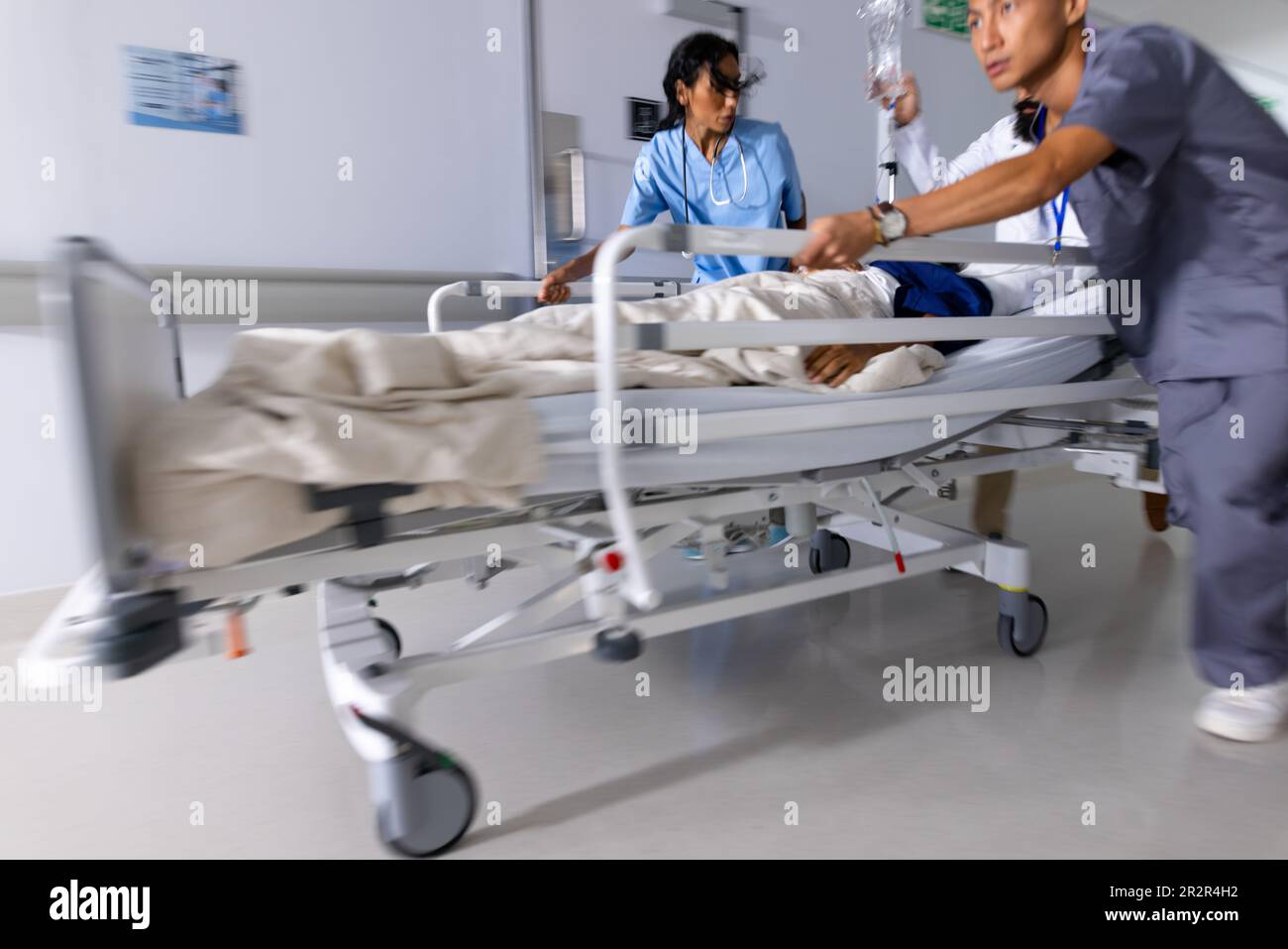 Diverse doctors urgently pushing patient lying in bed in corridor at ...