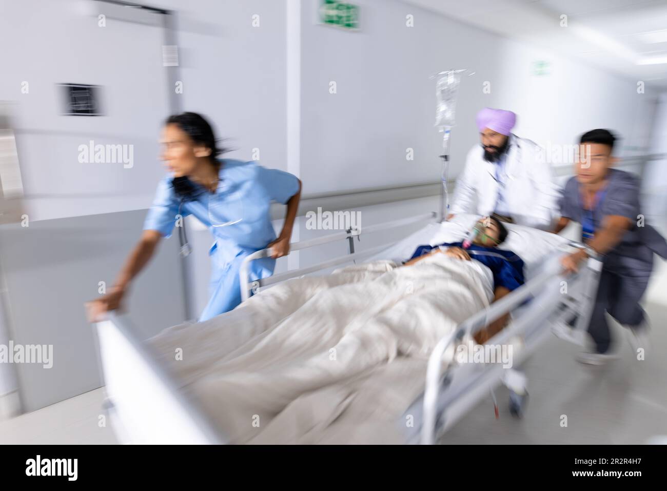 Diverse doctors urgently pushing patient lying in bed in corridor at ...