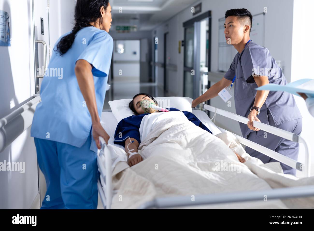 Diverse male and female doctor pushing female patient lying in bed in ...