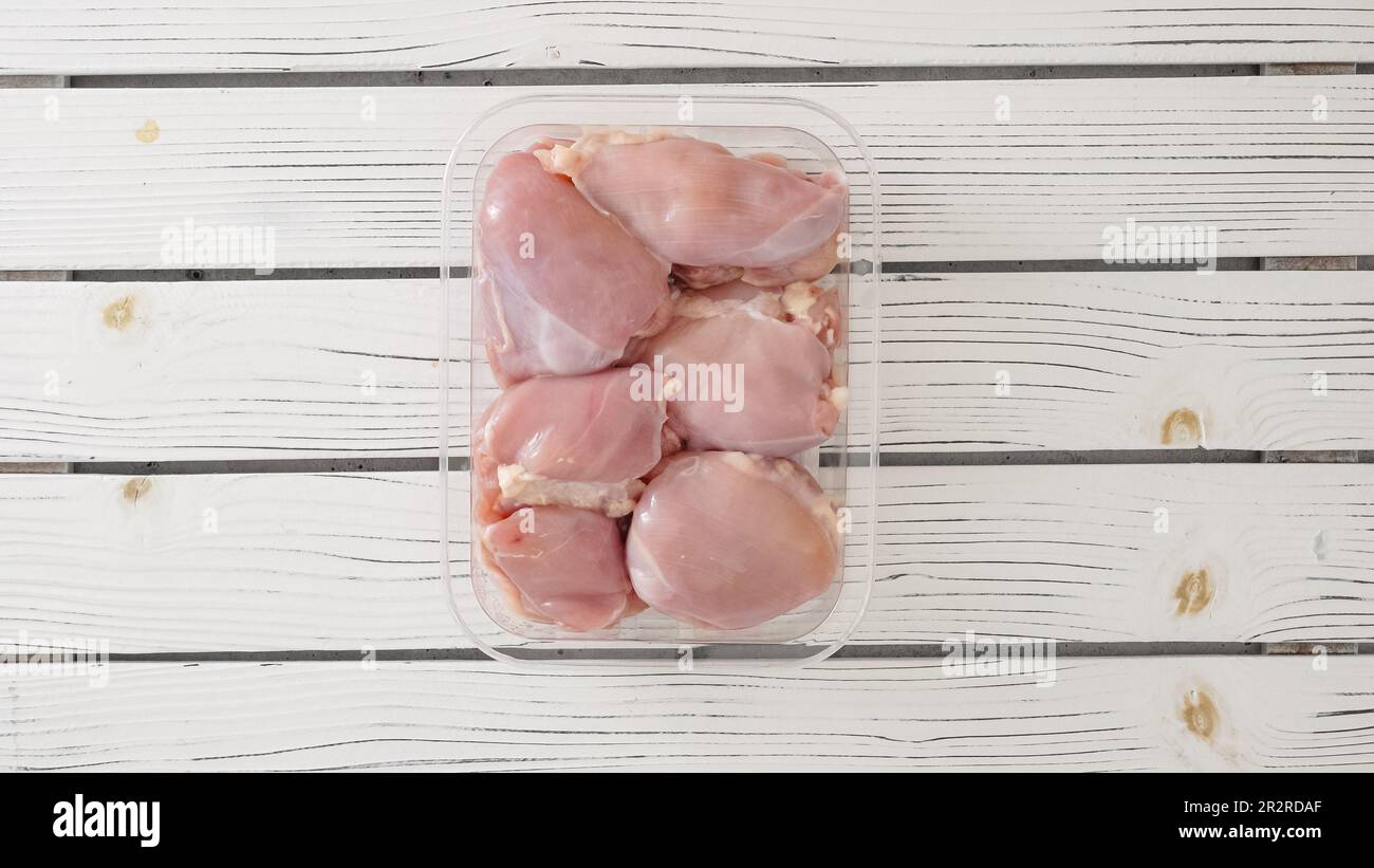Raw skinless boneless chicken thighs in plastic container close-up on ...