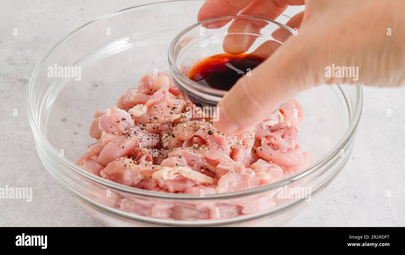 Adding soy sauce to chopped chicken fillet . Glass bowl with the ...