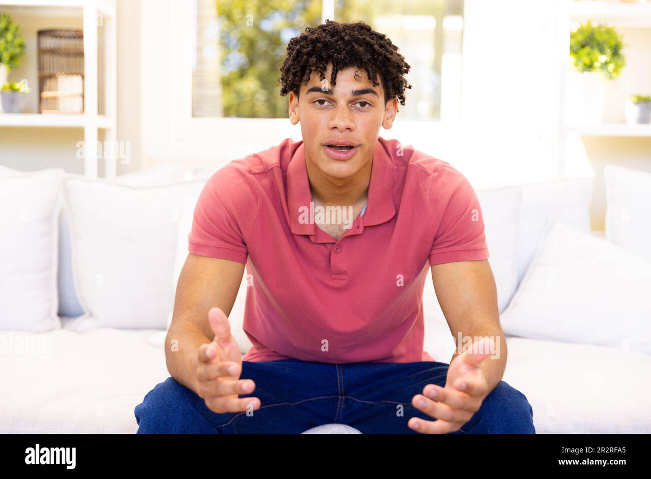 Portrait of biracial young man with dreadlocks gesturing and looking at ...