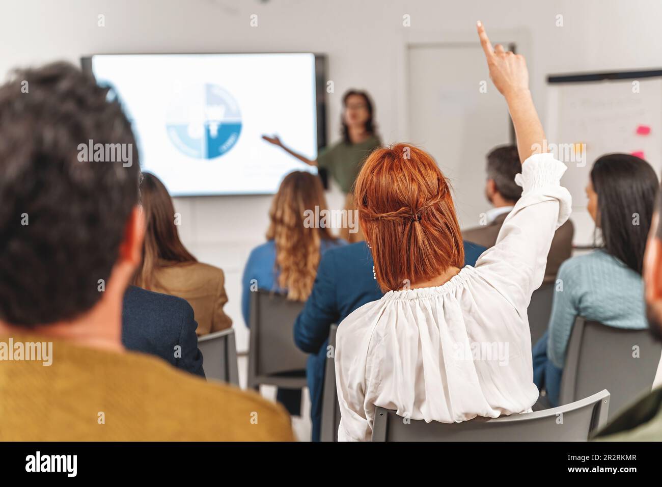 Businesswoman with red hair raising hand to ask question during a SWOT ...