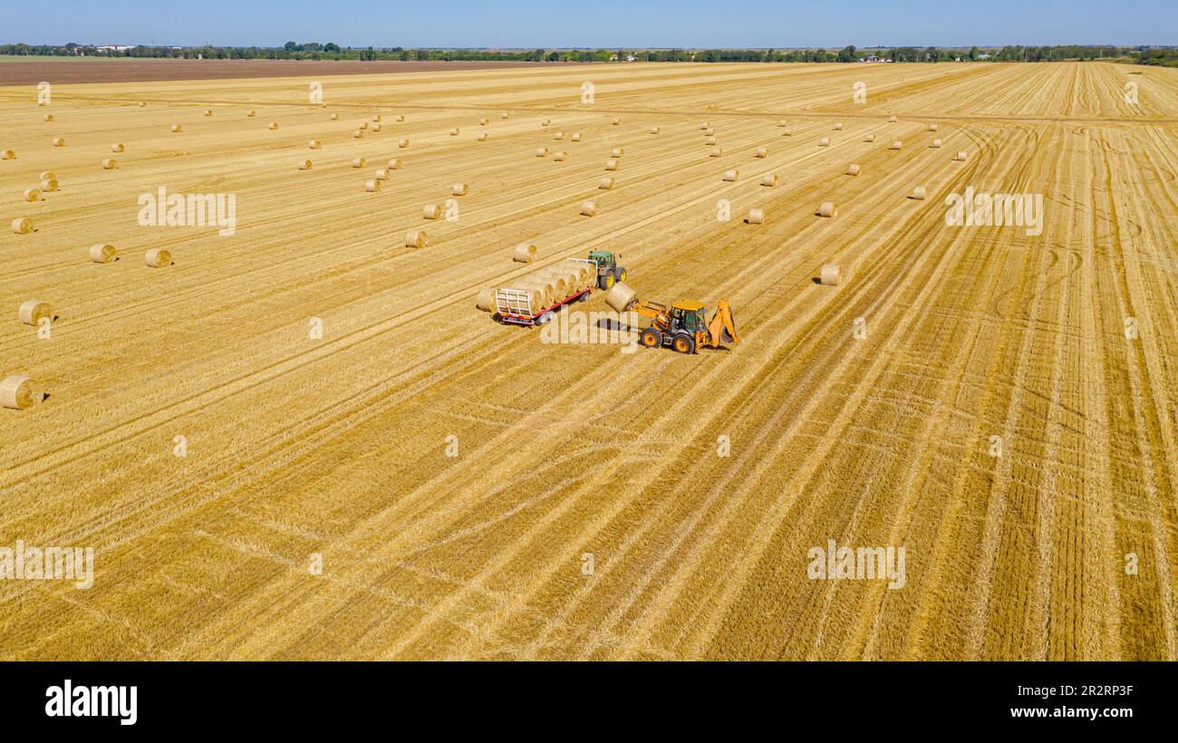 Above view on excavator as loading straw bales on trailer, tow by ...