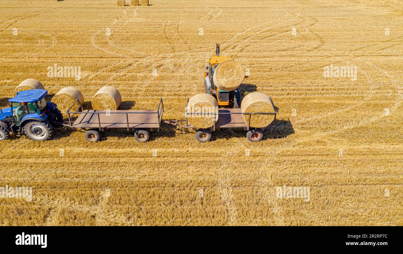 Above view on excavator as loading straw bales on trailer, tow by ...